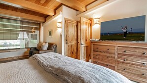 Quarto com uma cama grande, vigas de madeira no teto, cômoda de madeira e uma pintura de um campo de golfe.
