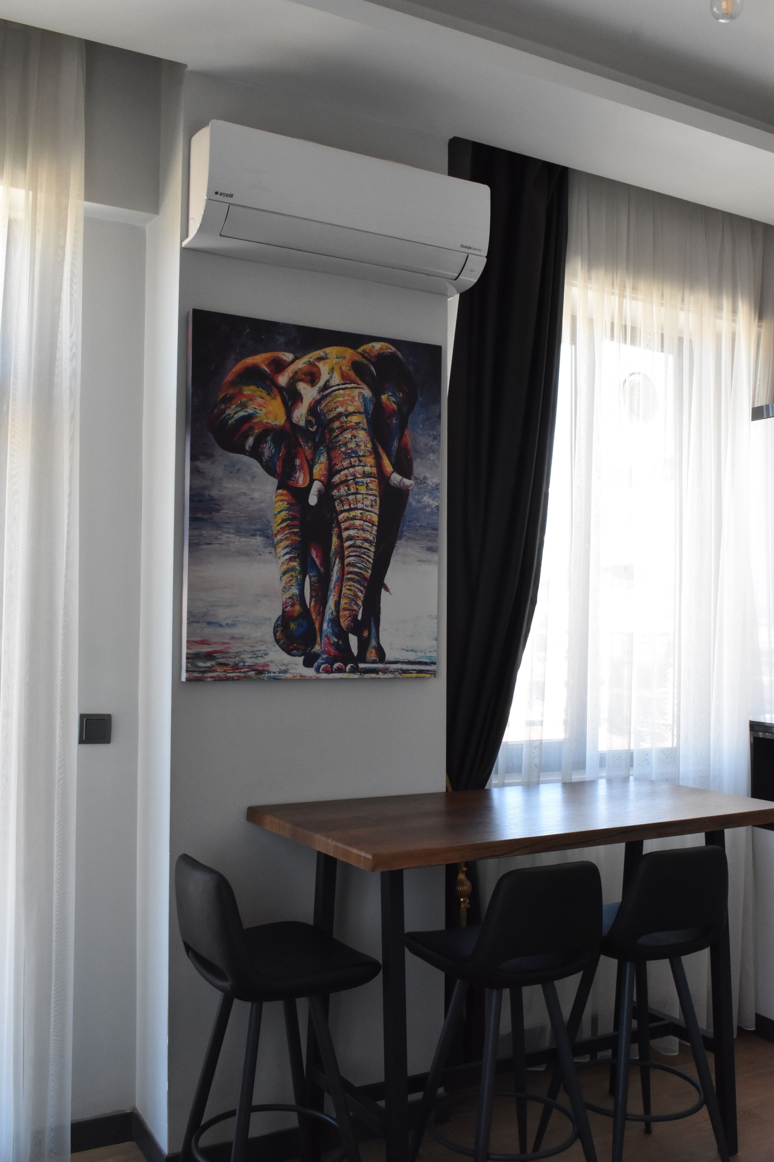 Uma área de refeições com uma mesa e cadeiras, um quadro de um elefante e um aparelho de ar condicionado na parede.