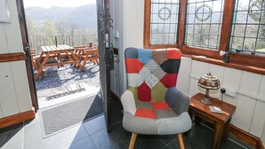 Um quarto aconchegante com uma cadeira de patchwork colorida, uma mesa de madeira com cadeiras do lado de fora e vista para montanhas pela janela.