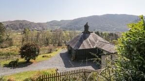 Um edifício rústico com telhado inclinado, cercado por um caminho de acesso de cascalho e uma cerca de madeira.