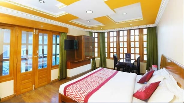 Quarto de hotel com uma cama grande, televisão na parede e vista para o exterior através de amplas janelas.