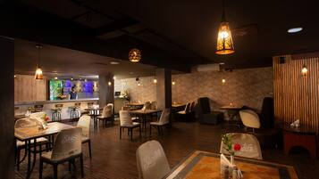 Restaurante com mesas e cadeiras de madeira, luminárias pendentes e uma parede de tijolos.