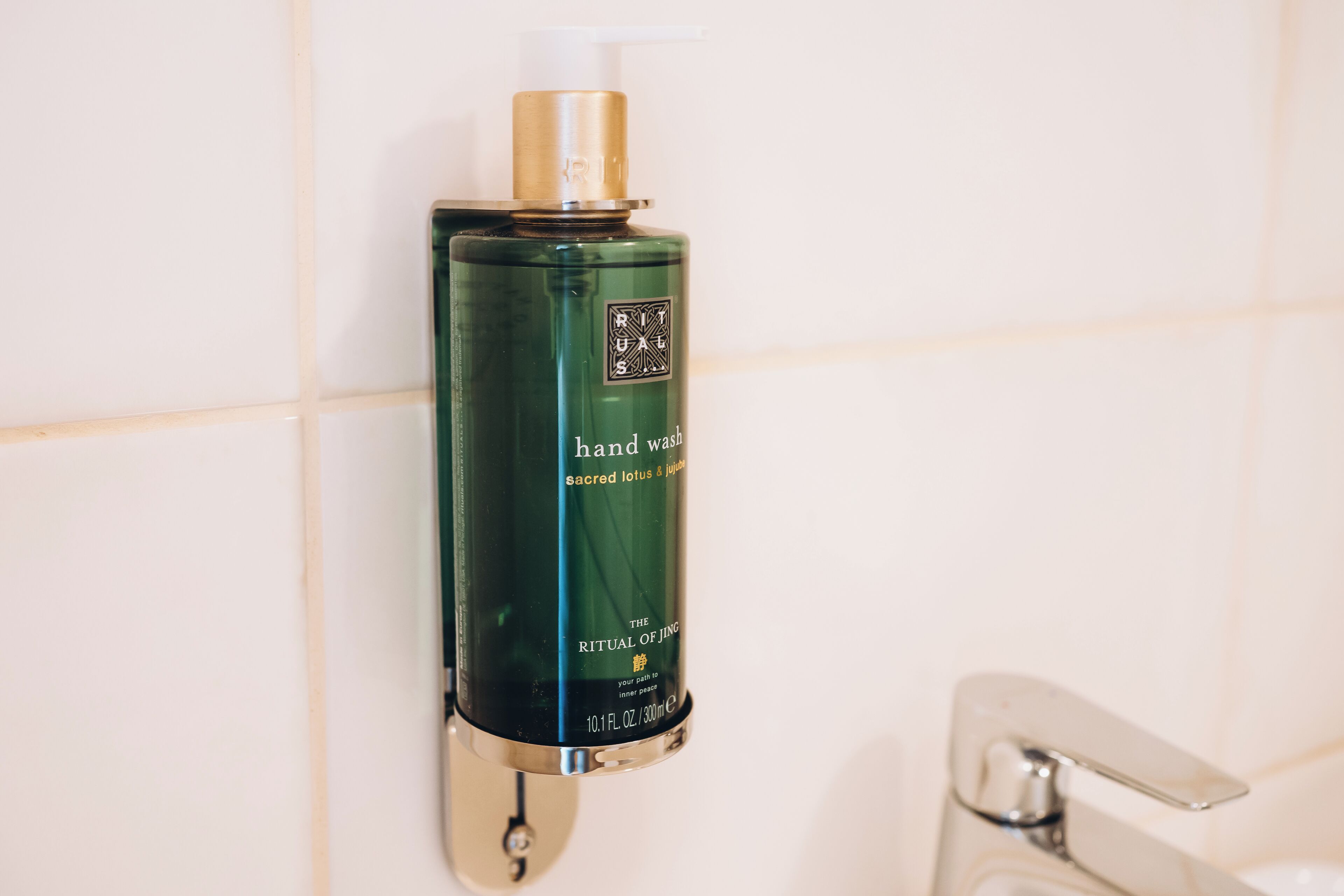 Dispensador de sabonete líquido fixado numa parede revestida de azulejos.