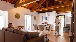 Ampla sala de estar com teto de madeira alto, área de jantar com mesa e cadeiras, e um sofá.