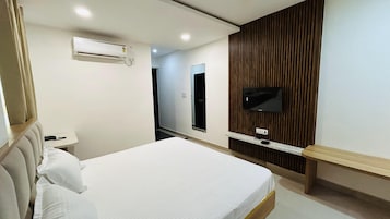 Quarto de hotel com cama, mesa de cabeceira, ar condicionado e televisão montada na parede.