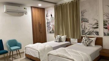 Quarto de hotel com duas camas de solteiro, um guarda-roupa de madeira, uma cadeira azul e arte floral na parede.