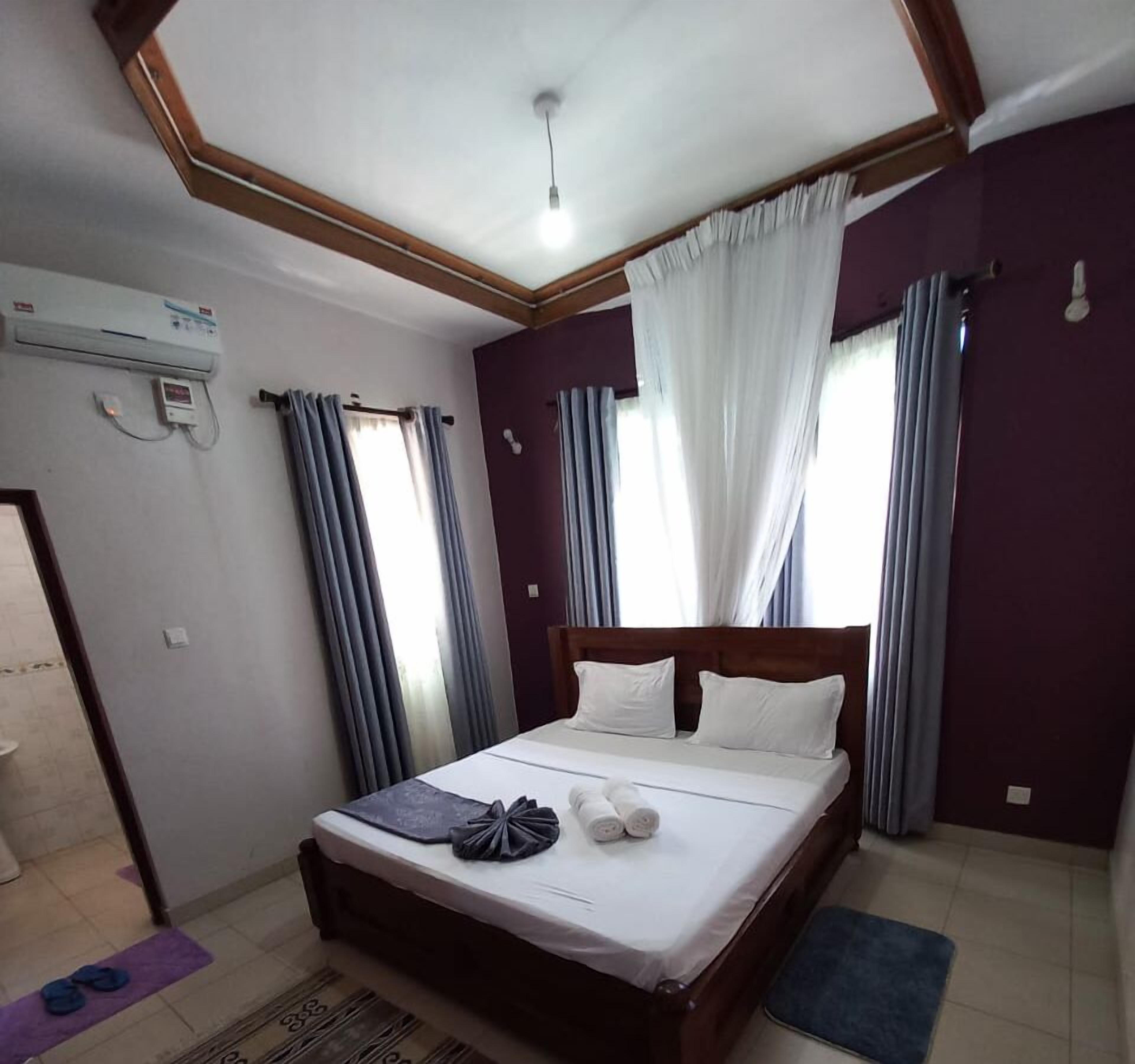 Quarto de hotel com cama, cortinas, ventoinha no teto e ar condicionado.
