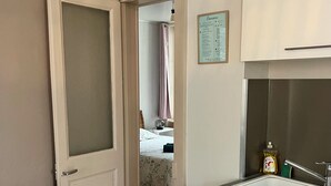 Quarto compacto com cozinha americana, uma cama com colcha florida e um banheiro visível através de uma porta aberta.