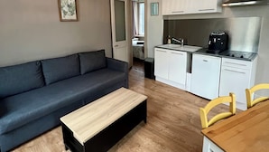 Um espaço de estar compacto com sofá, mesa de jantar, cozinha com fogão e armários, e luminária pendente.
