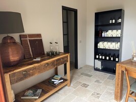Quarto com mesa de consola de madeira, uma luminária, livros e uma estante preta com garrafas.
