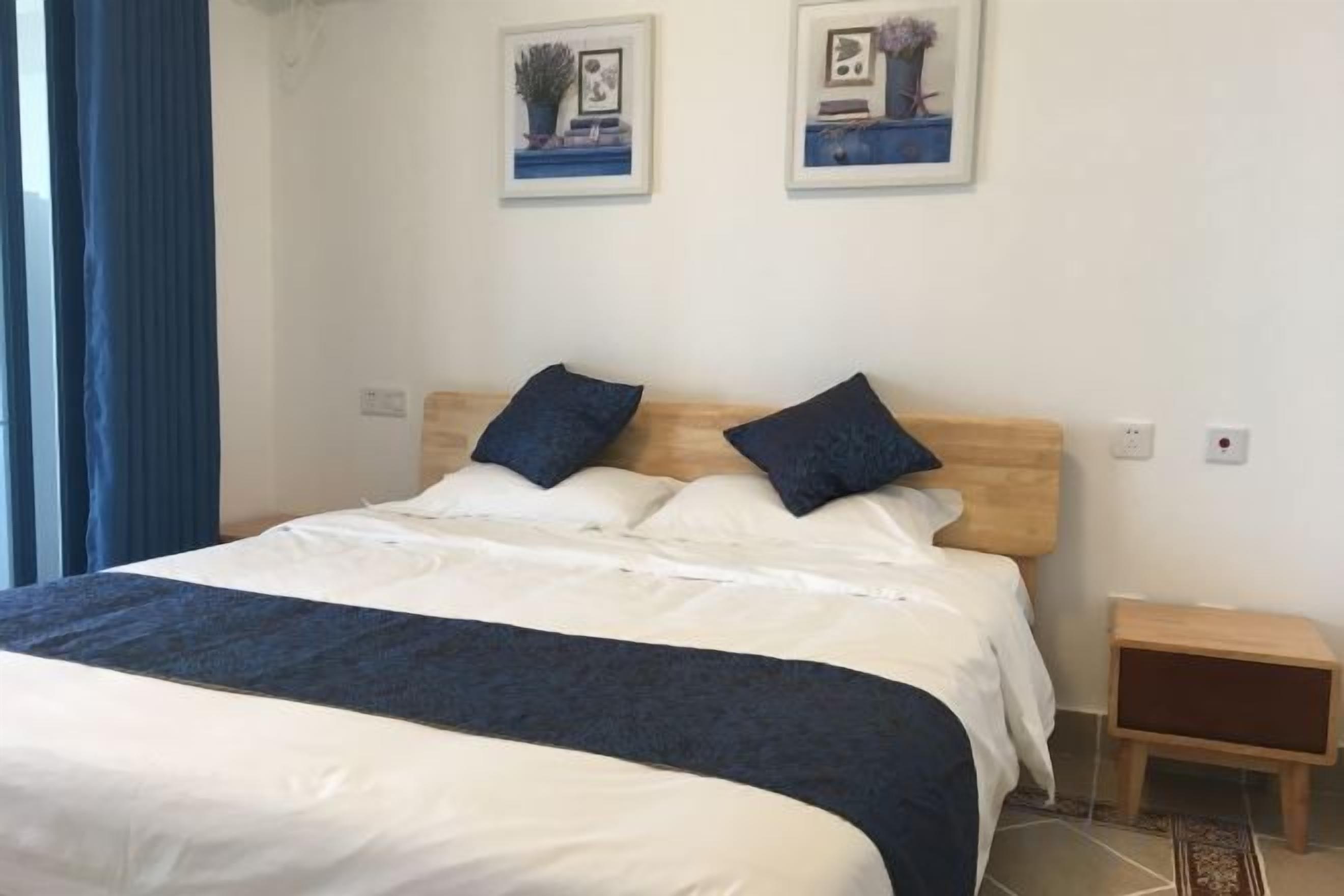 Cama bem arrumada com cabeceira de madeira, mesa de cabeceira e duas fotos emolduradas na parede.