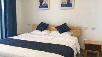 Cama bem arrumada com cabeceira de madeira, mesa de cabeceira e duas fotos emolduradas na parede.
