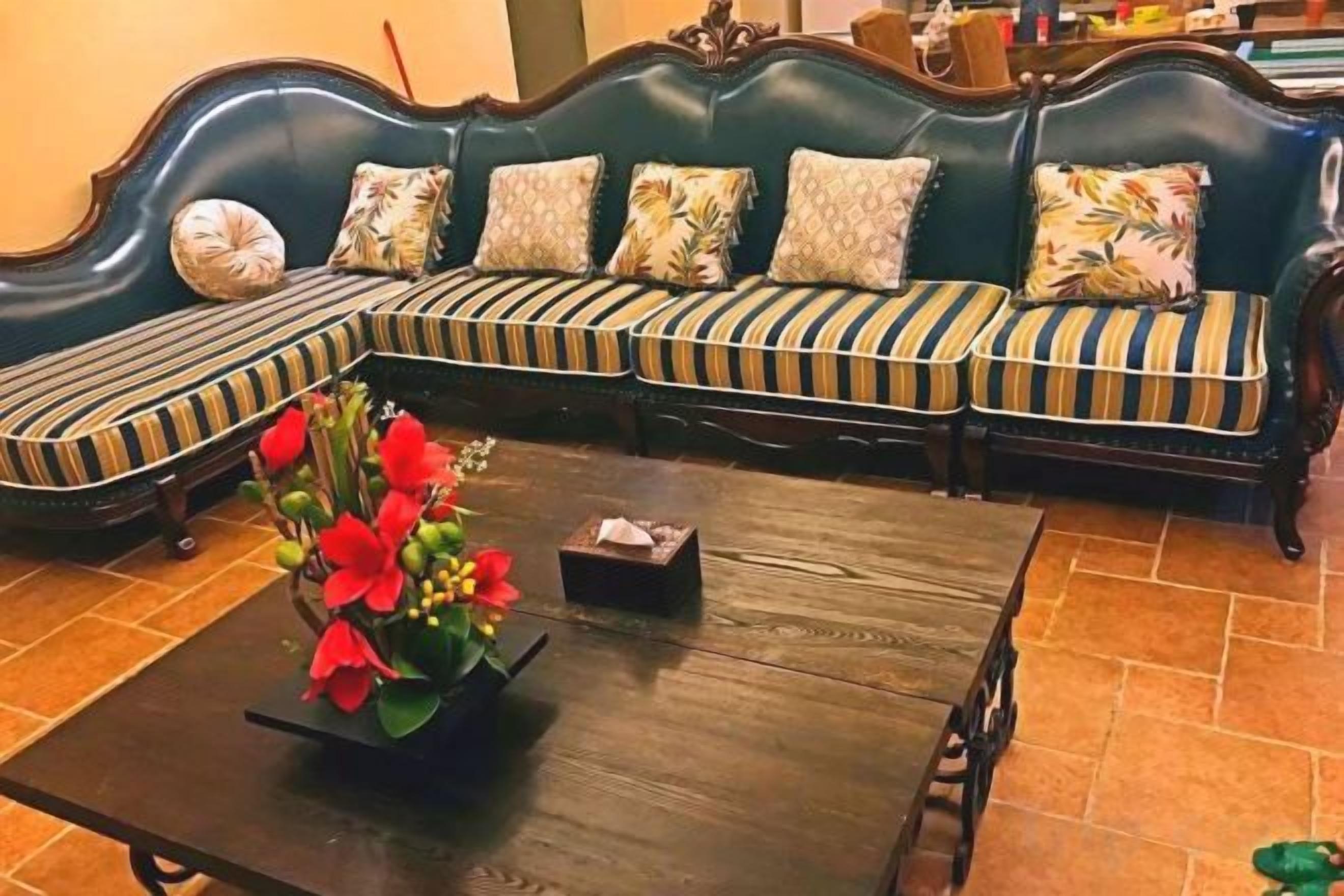 Um sofá modular com almofadas listradas, uma mesa de centro de madeira com um arranjo de flores, e um chão de azulejos.