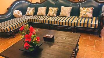 Um sofá modular com almofadas listradas, uma mesa de centro de madeira com um arranjo de flores, e um chão de azulejos.
