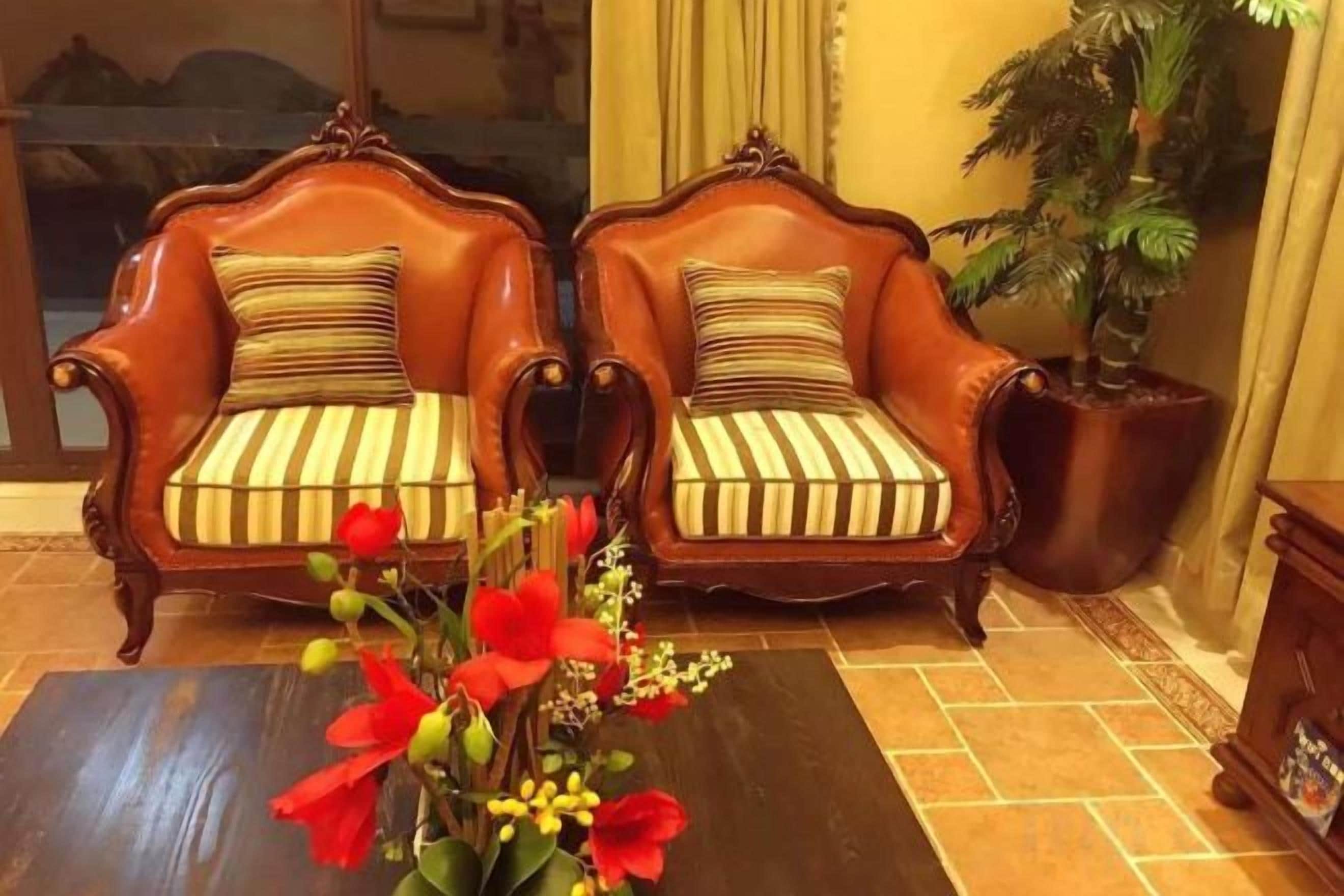 Duas poltronas estofadas com almofadas listradas, uma mesa de centro de madeira e um vaso com planta.