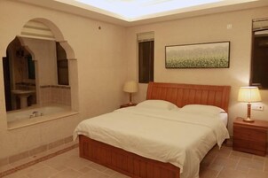 Quarto com cama, mesa de cabeceira, abajur, pintura e espelho.