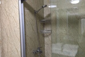 Box de vidro com chuveiro manual e torneira fixada na parede.