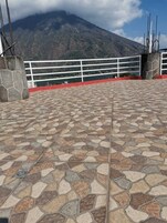 Um terraço com azulejos, uma parede de pedra e um corrimão, com vista para uma paisagem montanhosa.