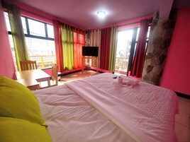 Quarto de hotel com cama, uma cadeira, televisão e janela com cortinas.