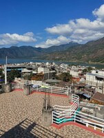 Vista de uma cidade costeira com edifícios residenciais e comerciais, céu azul límpido e montanhas ao fundo.