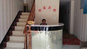 Área de recepção de hotel, com escadaria, balcão de atendimento e parede com caracteres chineses.