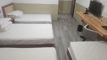 Quarto de hotel com três camas de solteiro, uma escrivaninha de madeira com televisão e um pequeno cesto de lixo.