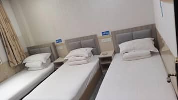 Quarto de hotel com três camas de solteiro, cada uma com uma almofada e uma mesa de cabeceira.