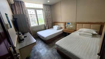 Quarto de hotel com duas camas de solteiro, uma secretária pequena com chaleira, janela com cortinas e ar condicionado fixado na parede.