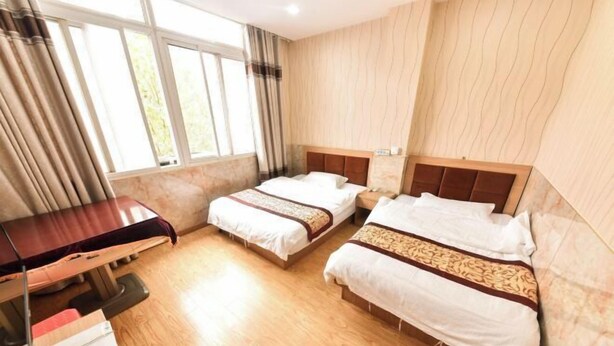 Quarto de hotel com duas camas, uma escrivaninha e uma janela com cortinas.