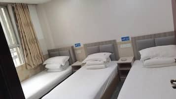 Quarto de hotel com três camas de solteiro, cada uma com roupa de cama e almofadas brancas, uma mesa de cabeceira e um criado-mudo.