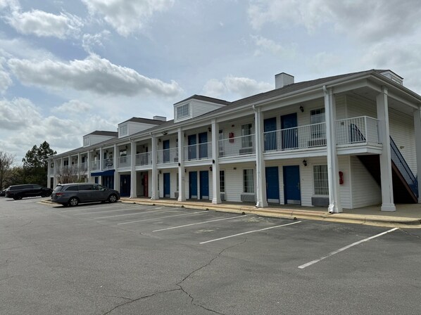 Um motel de vários andares com um pátio central, varandas e estacionamento.