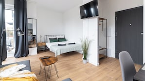 Quarto moderno com cama, mesa de cabeceira e uma grande janela com cortinas.