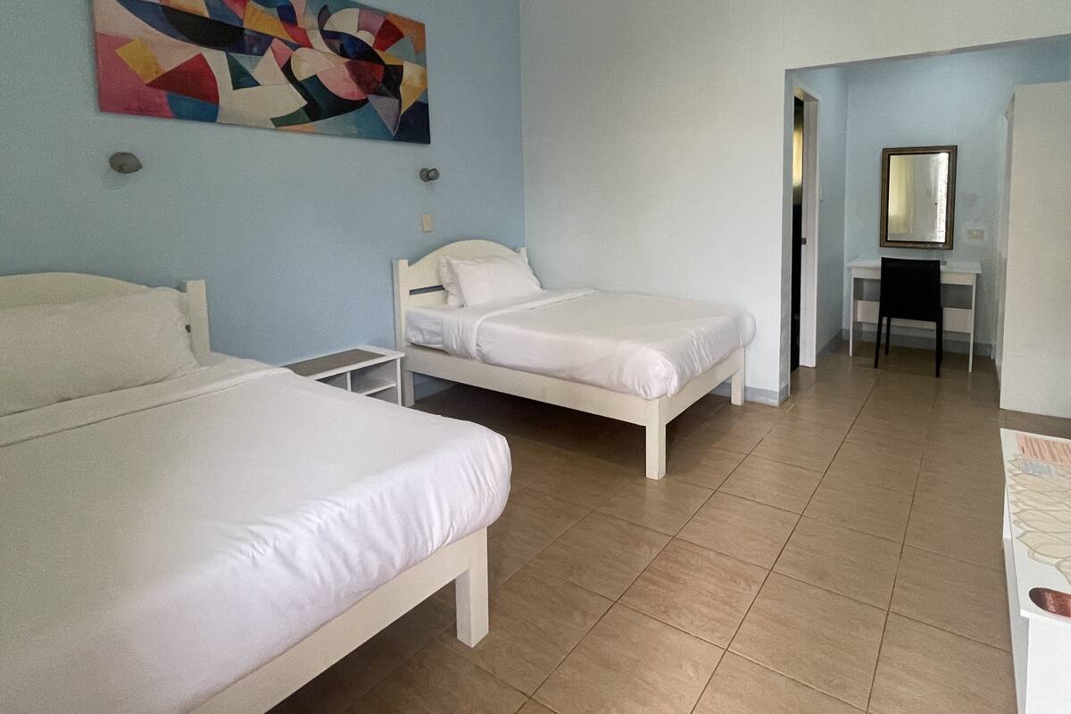 Quarto de hotel com duas camas, uma escrivaninha e uma pintura abstrata colorida na parede.