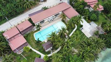 Vista aérea de um resort com vários edifícios, piscina e palmeiras ao redor.