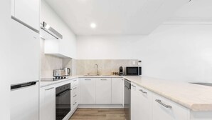 Uma cozinha moderna com armários brancos, piso de madeira e bancada de mármore.