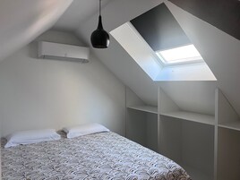 Quarto com claraboia, cama com roupa de cama estampada e ar condicionado branco.