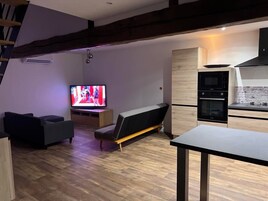 Uma sala de estar moderna com sofá, televisão e cozinha equipada com micro-ondas e forno.