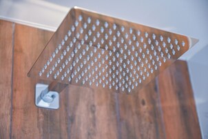 Um chuveiro de metal com vários orifícios, fixado numa parede de madeira.