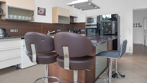 Uma cozinha moderna com dois bancos de bar, um micro-ondas e uma geladeira de aço inoxidável.
