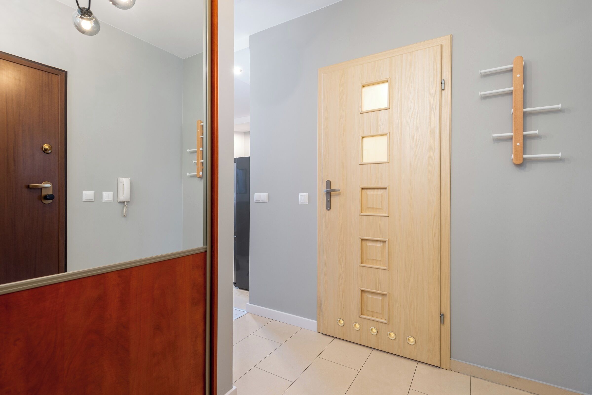 Um corredor com uma porta de madeira, um porta-toalhas na parede e um interruptor de luz.