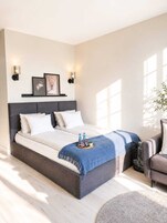 Quarto moderno com uma cama grande, abajures, quadros emoldurados e uma pequena planta.