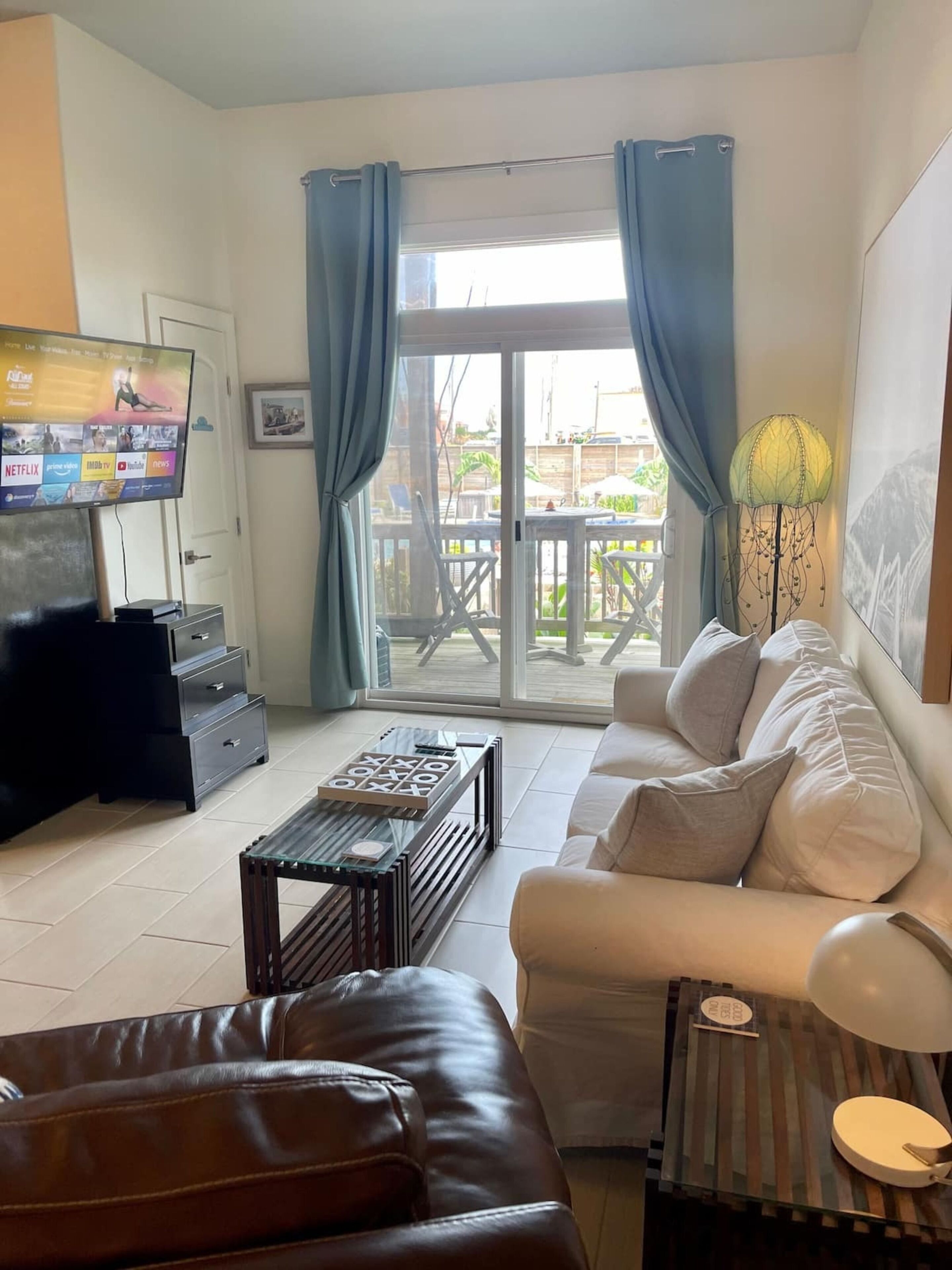 Uma sala de estar com sofá, mesa de centro, televisão e porta de vidro deslizante que dá para uma área externa.