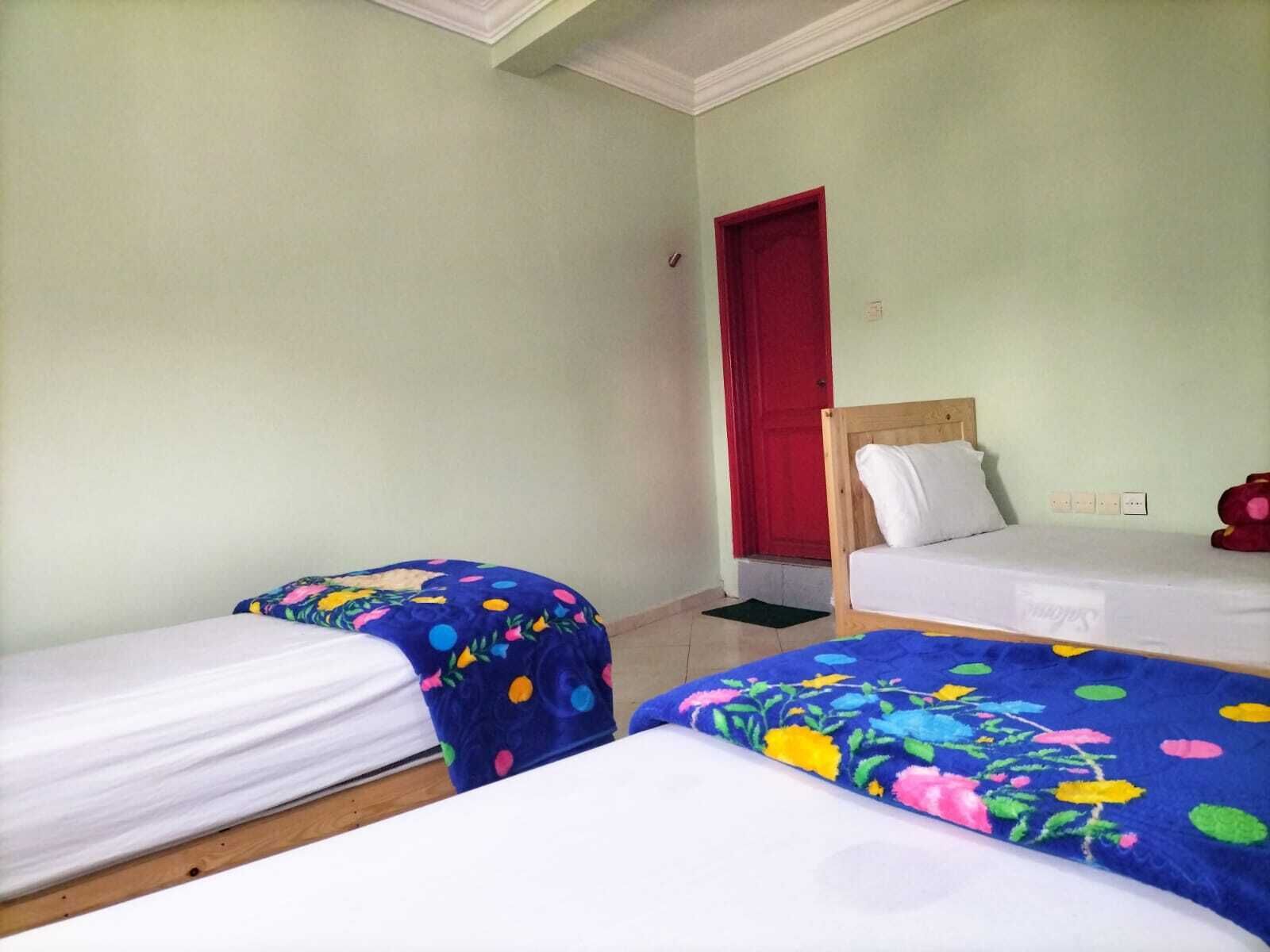 Quarto com duas camas, uma porta vermelha e um tapete pequeno.