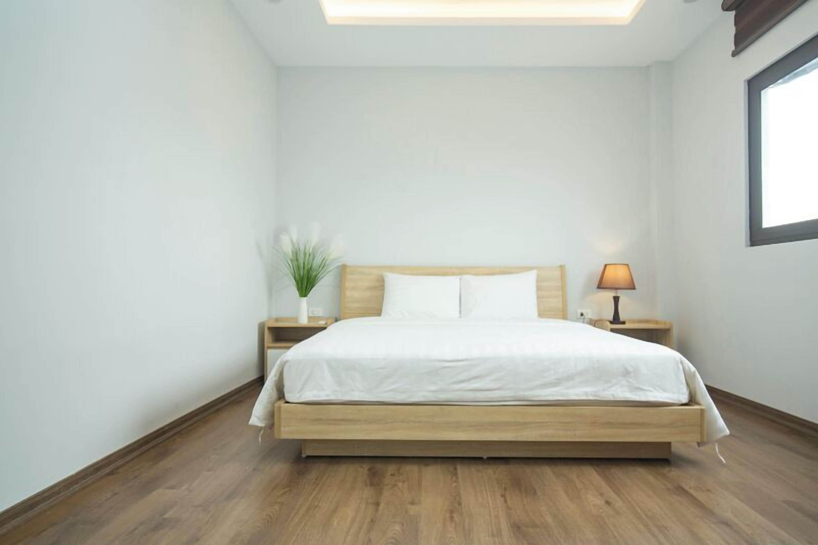 Cama bem arrumada com lençóis brancos, cabeceira de madeira e duas mesas de cabeceira com luminárias.