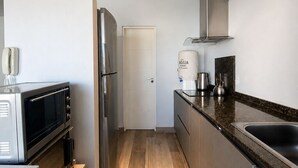 Uma cozinha moderna com micro-ondas, forno e frigorífico embutidos. Há uma máquina de café e uma pia na bancada.