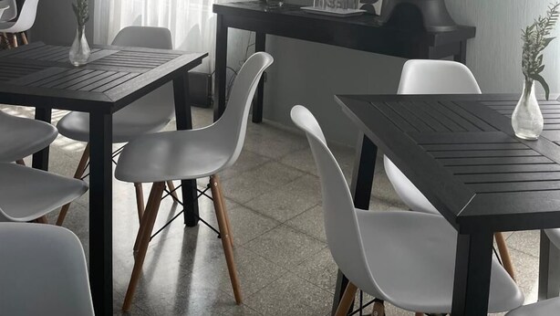 Uma sala de jantar moderna com uma mesa preta e cadeiras brancas, um espelho grande e uma janela com cortinas leves.