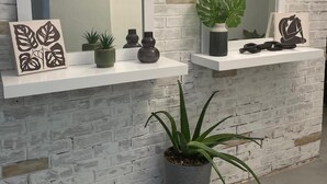 Um interior moderno com duas molduras brancas em espelhos acima de prateleiras brancas, cada uma com objetos decorativos e plantas.