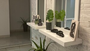 Uma área de recepção com parede de tijolos brancos, um espelho grande e uma prateleira com objetos decorativos e plantas.