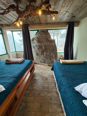 Quarto com duas camas, uma grande formação rochosa e vista pela janela.