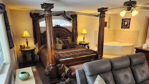 Quarto com cama de dossel, área de estar com sofá, uma pequena mesa com um vaso e uma banheira.